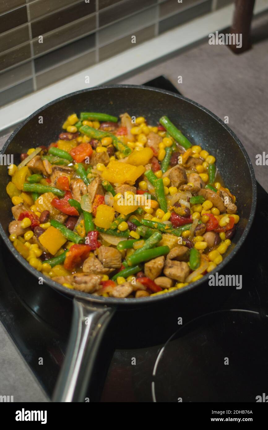 A vertical shot of a chicken dish with fried vegetables in a frying pan ...