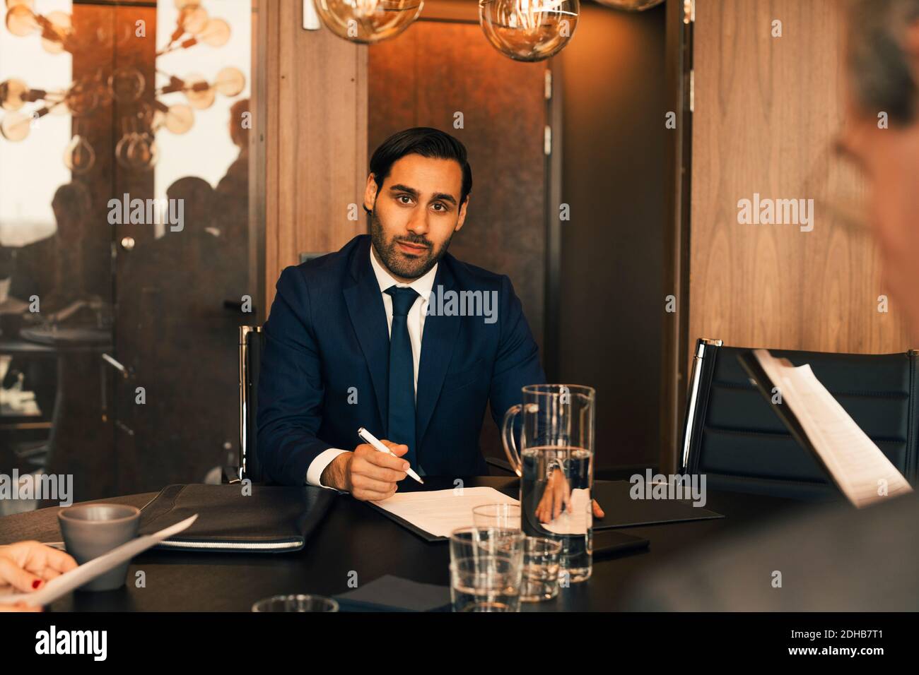 Portrait of confident mid adult lawyer with documents at conference ...