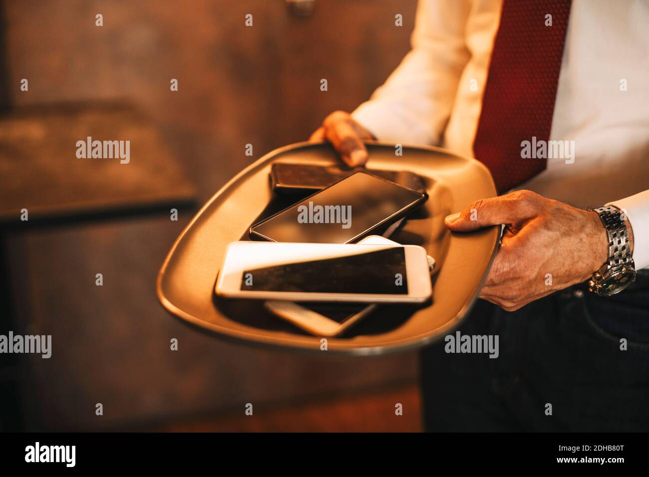 Midsection of male professional holding smart phones in tray at office ...