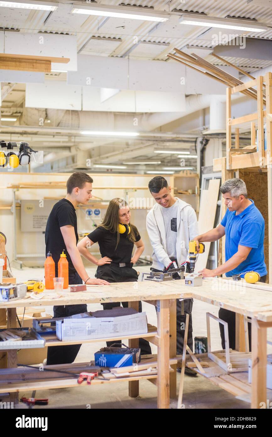 Male carpenter explaining power drill to trainees at workbench during ...