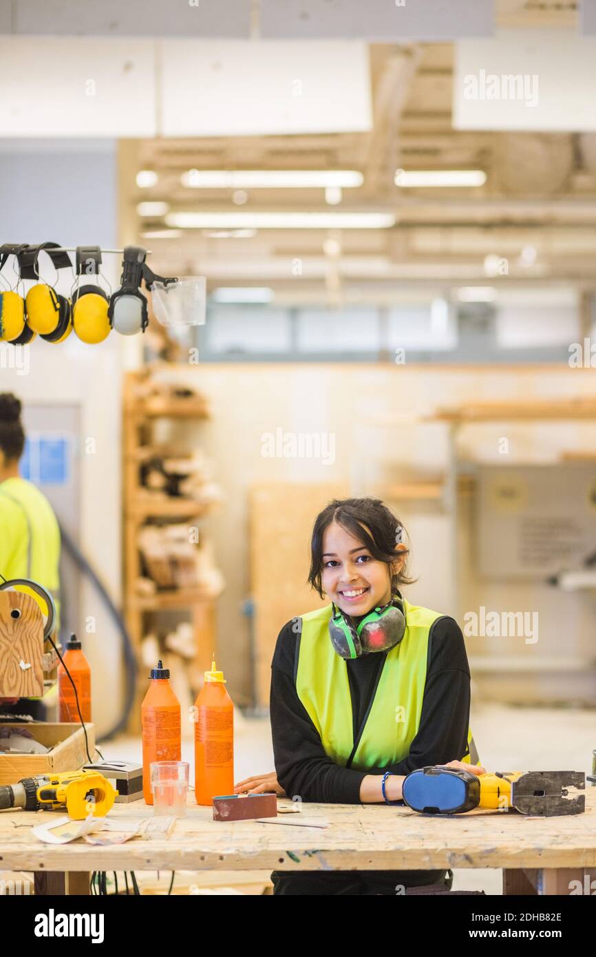 Portrait of smiling young female trainee leaning on workbench at ...