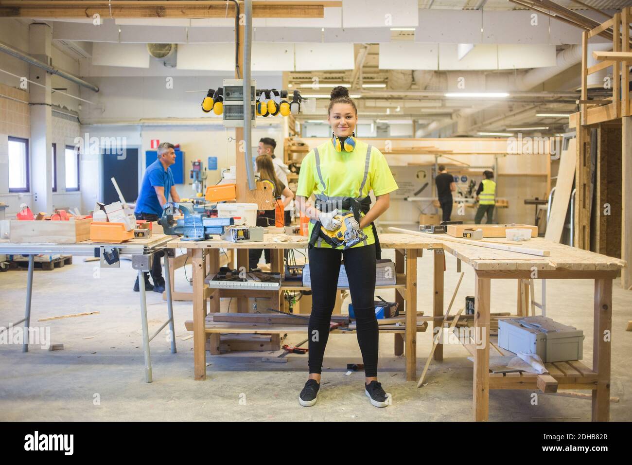 Full length portrait of smiling young female trainee holding power tool ...