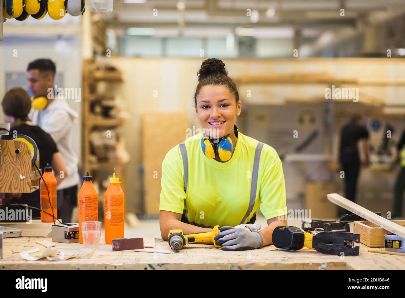 Smiling young female trainee leaning on workbench at illuminated ...