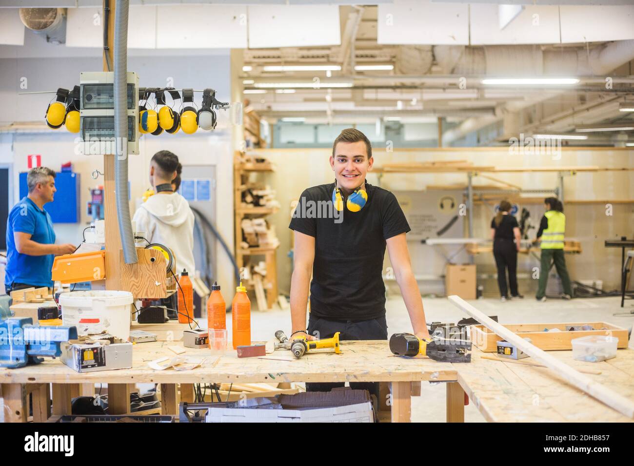 Portrait of confident young trainee standing at workbench at ...