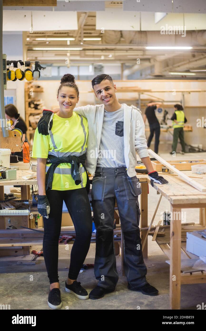 Full length portrait of smiling female trainee standing with arm around ...