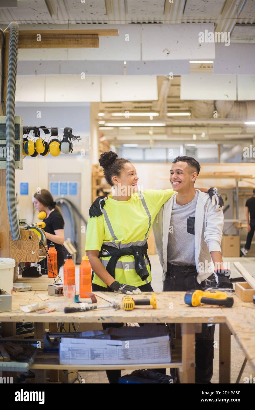 Cheerful female trainee standing with arm around male coworker at ...