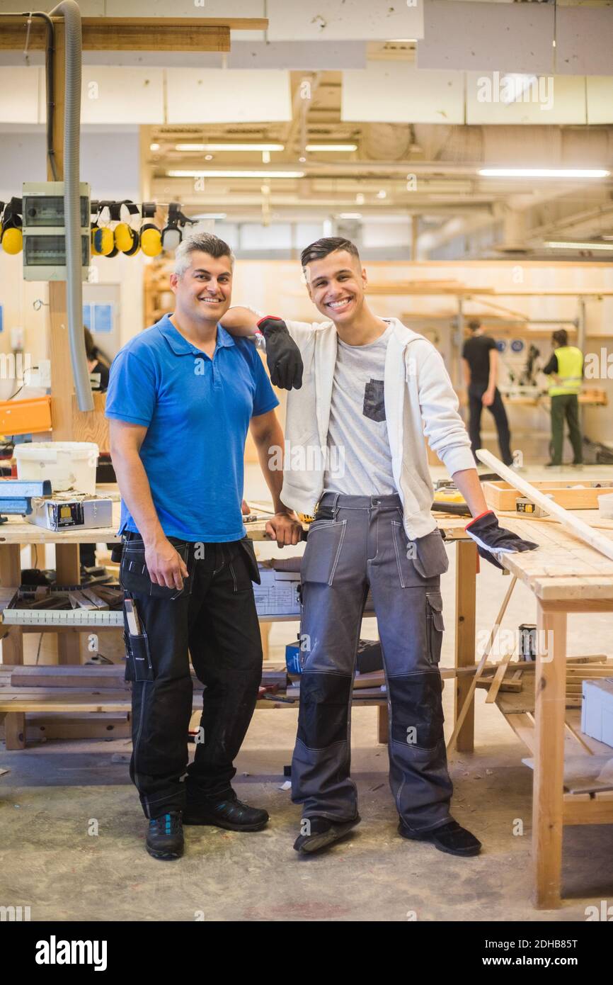Full length portrait of smiling teenage trainee standing with hand on ...