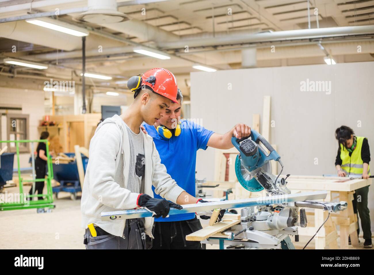 Teenage carpenter using level while standing by instructor with ...
