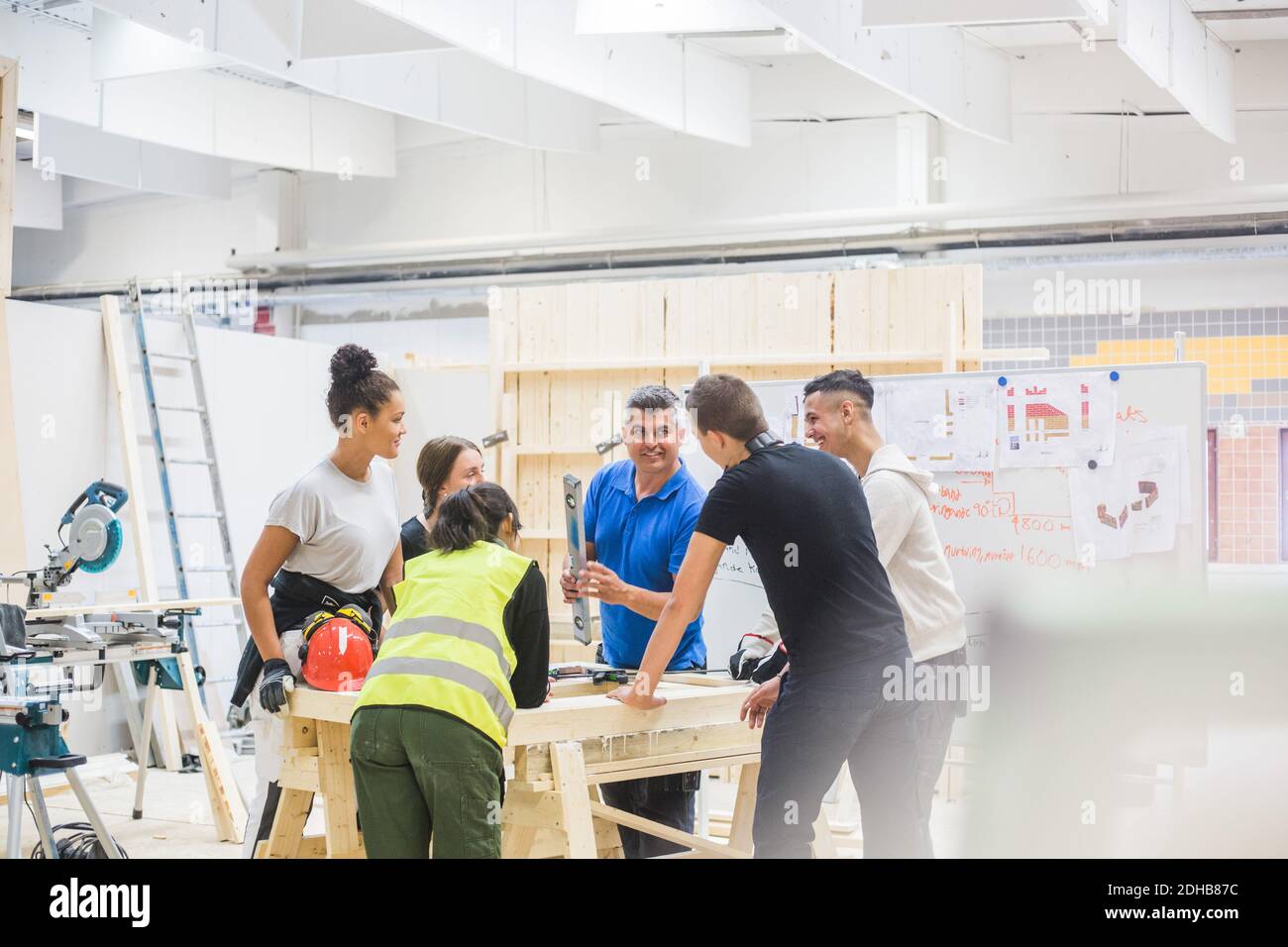 Male instructor teaching about level to trainees standing at workbench ...
