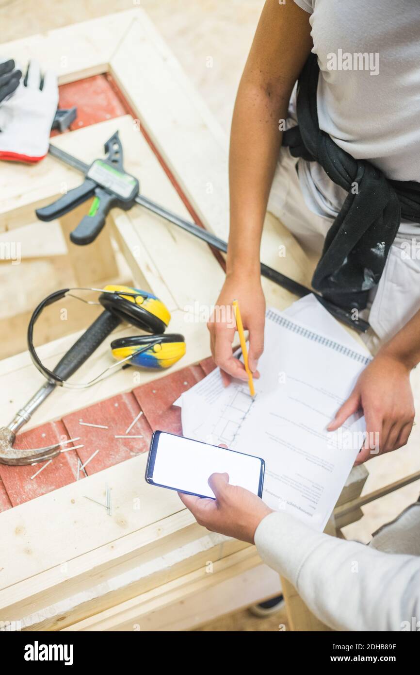 Teenage trainee holding smart phone by coworker drawing diagram on ...
