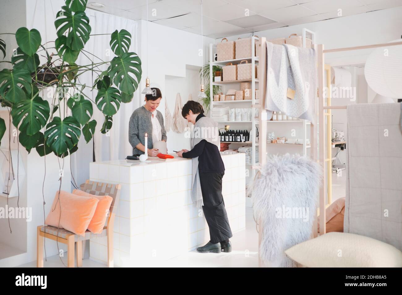 Female customer using mobile phone in front of owner at upholstery shop ...