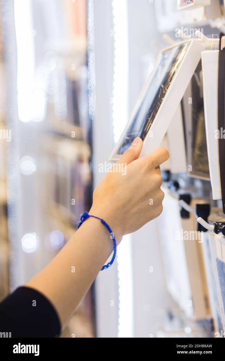 Hand of young female customer holding phone cover box hanging from rack ...