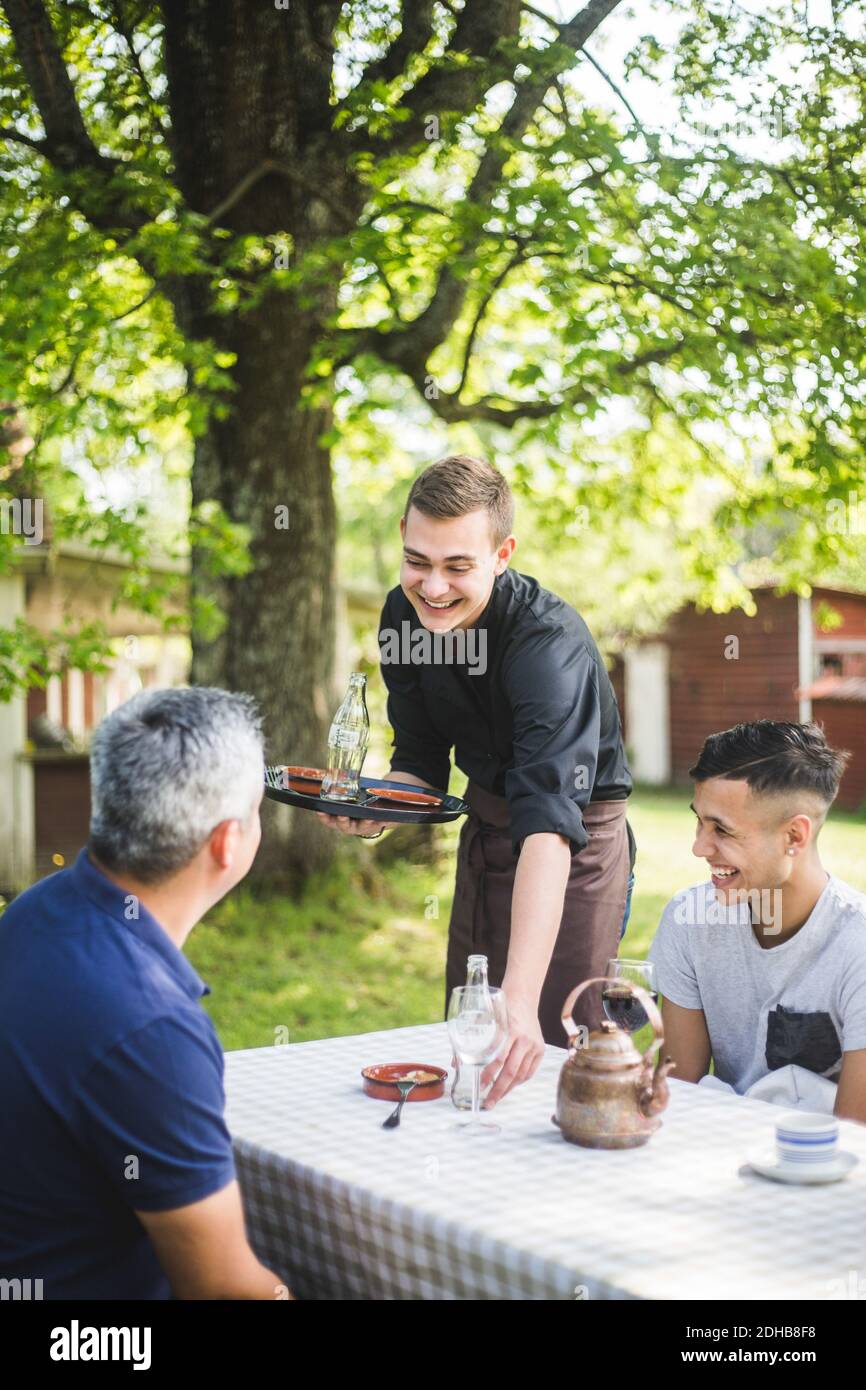 Smiling young waiter talking with customers while working at outdoor ...