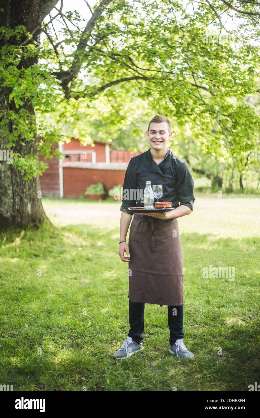 Full length portrait of smiling confident young waiter standing on ...