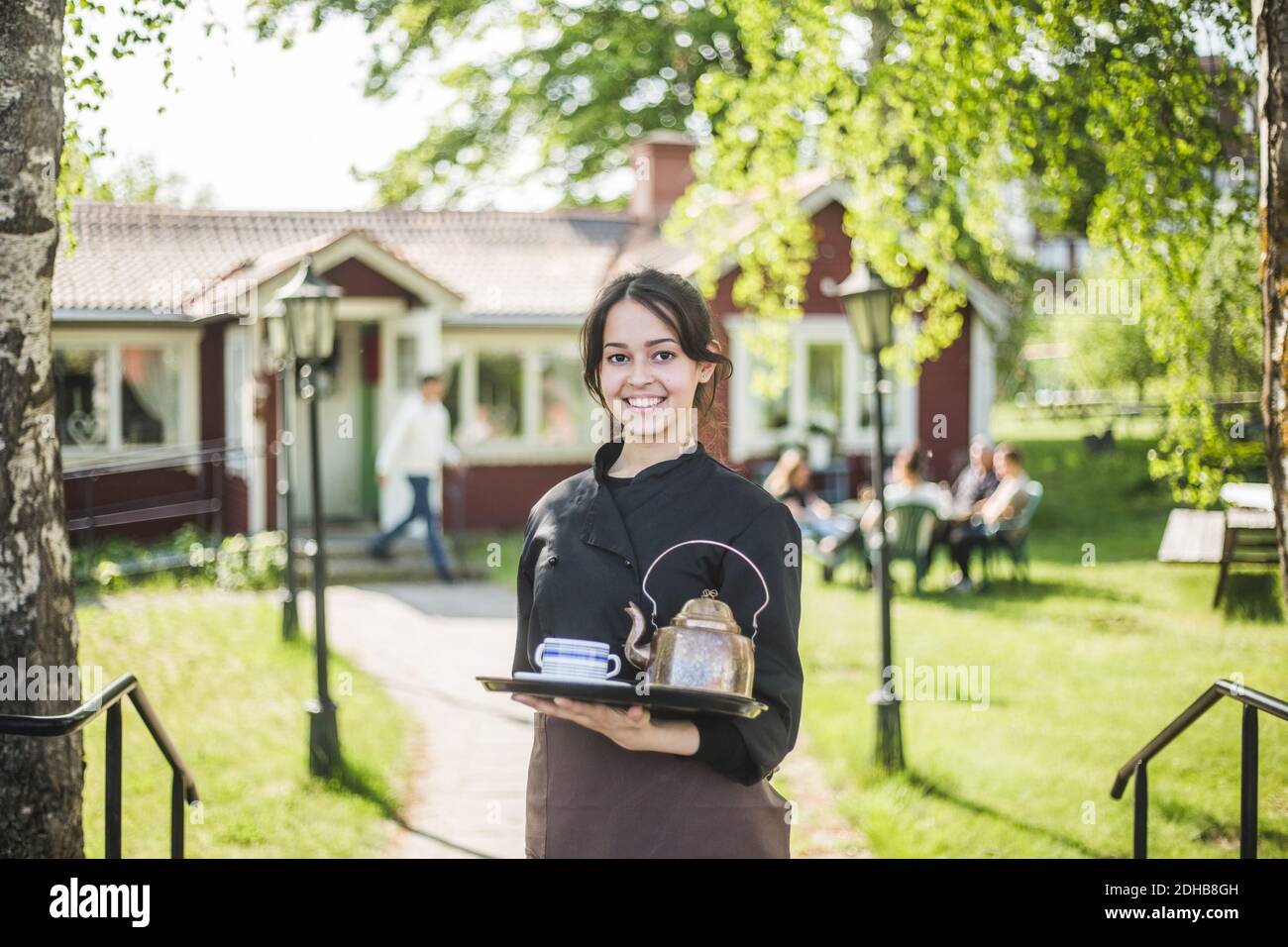 Portrait of confident young female waitress smiling while holding ...