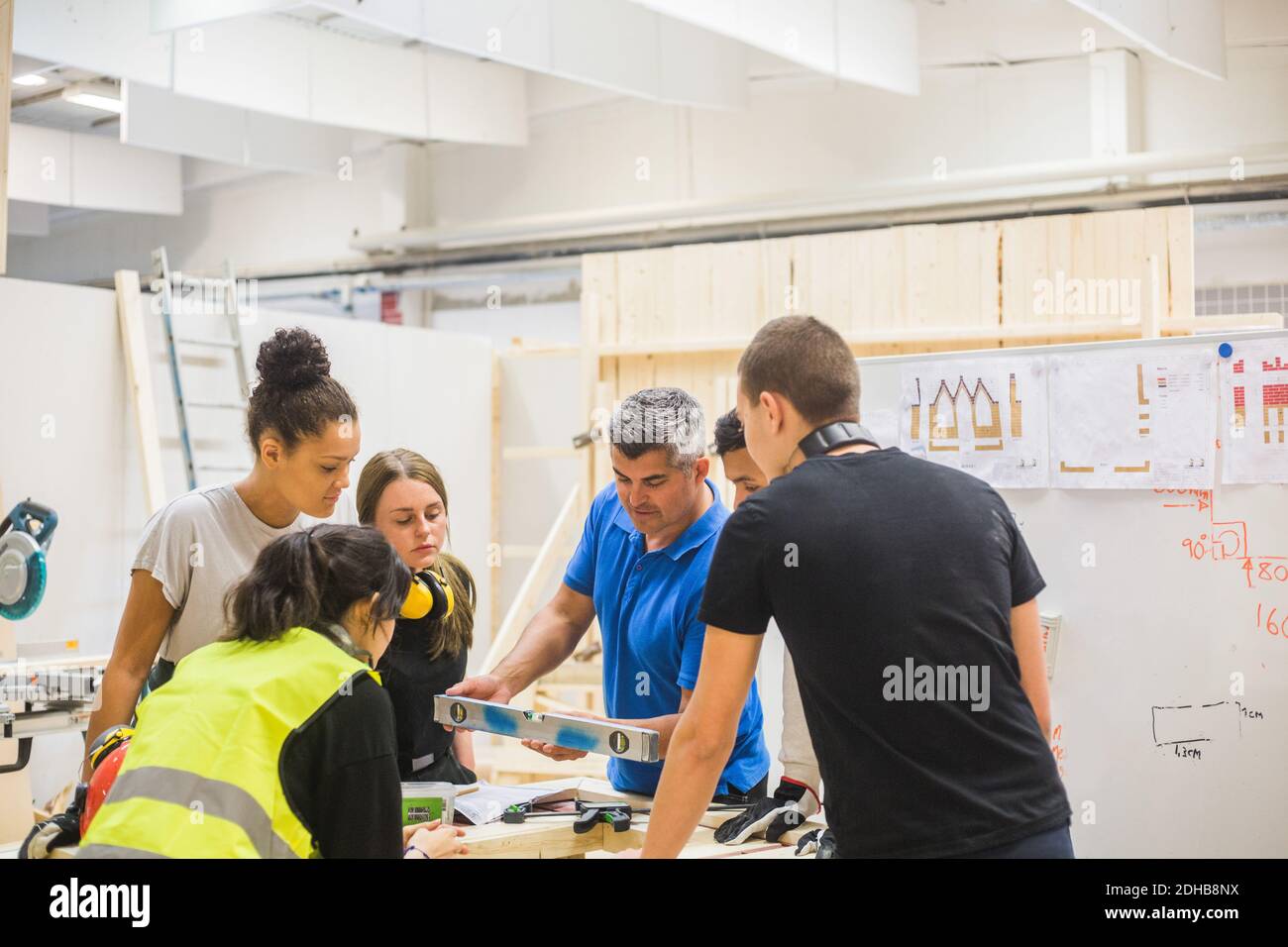 Male instructor using level amidst trainees at workbench in illuminated ...
