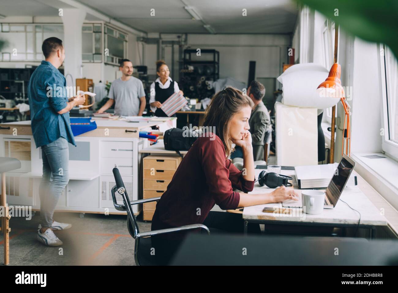 Creative businesswoman using laptop at desk while colleagues working in ...