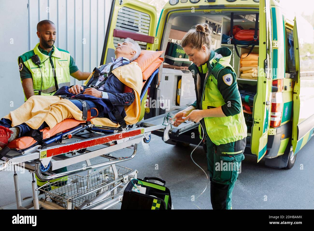 Paramedic with patient looking at coworker preparing oxygen equipment ...