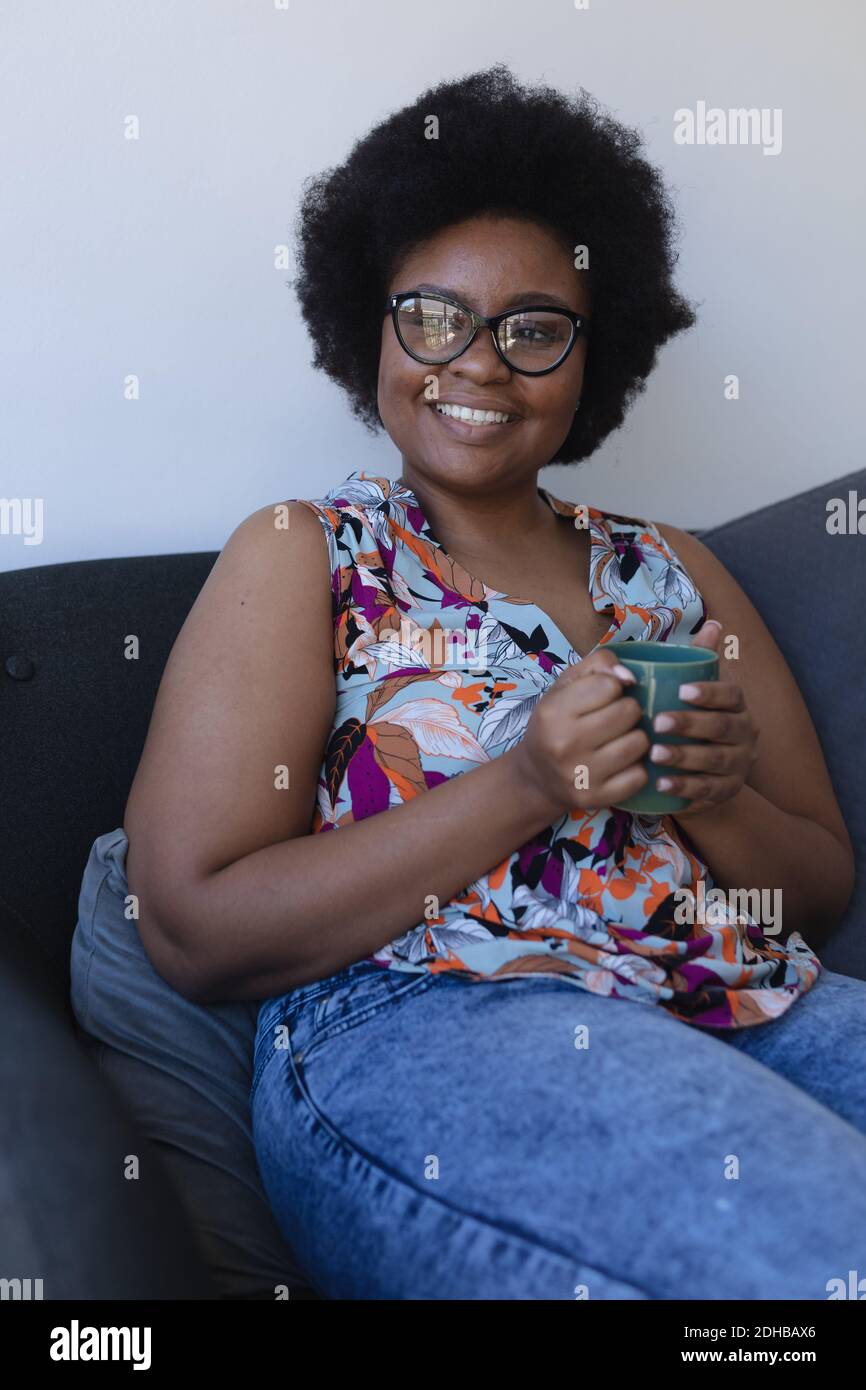 Midsection of african american woman sitting on couch drinking cup of ...