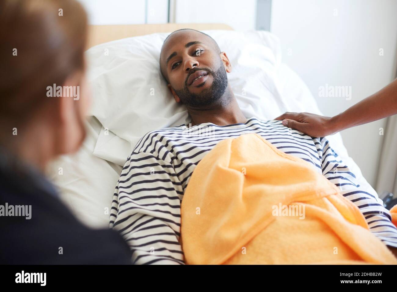 Young patient looking at friend while lying on bed in ward at hospital ...