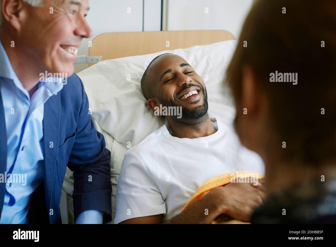 Smiling young patient with eyes closed lying on bed at hospital ward ...