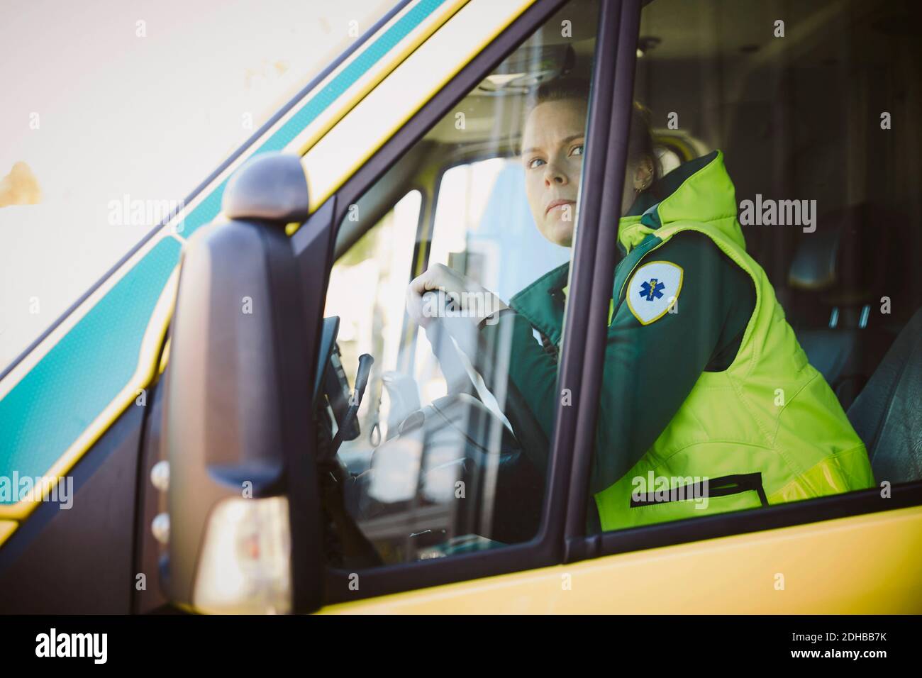 Female thoughtful rescue worker looking away while sitting in ambulance ...