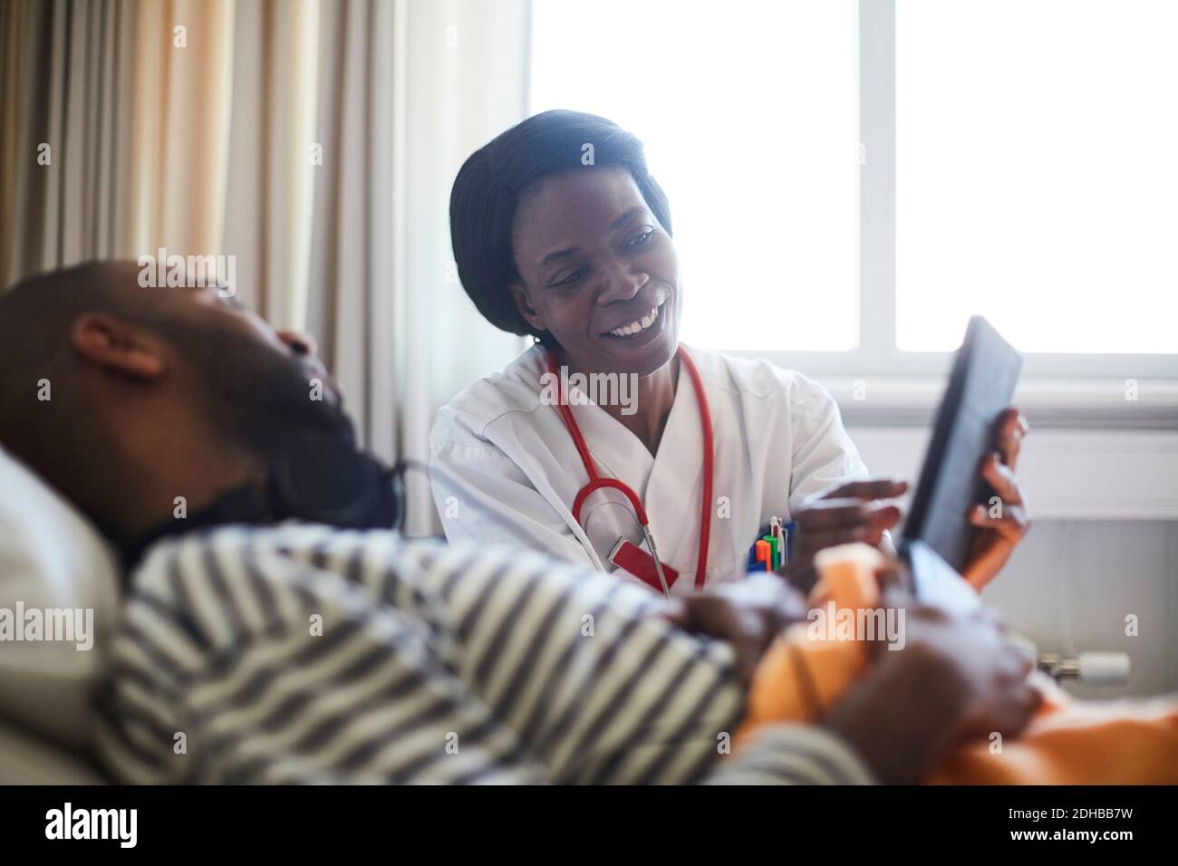 Smiling healthcare worker showing digital tablet to patient during ...