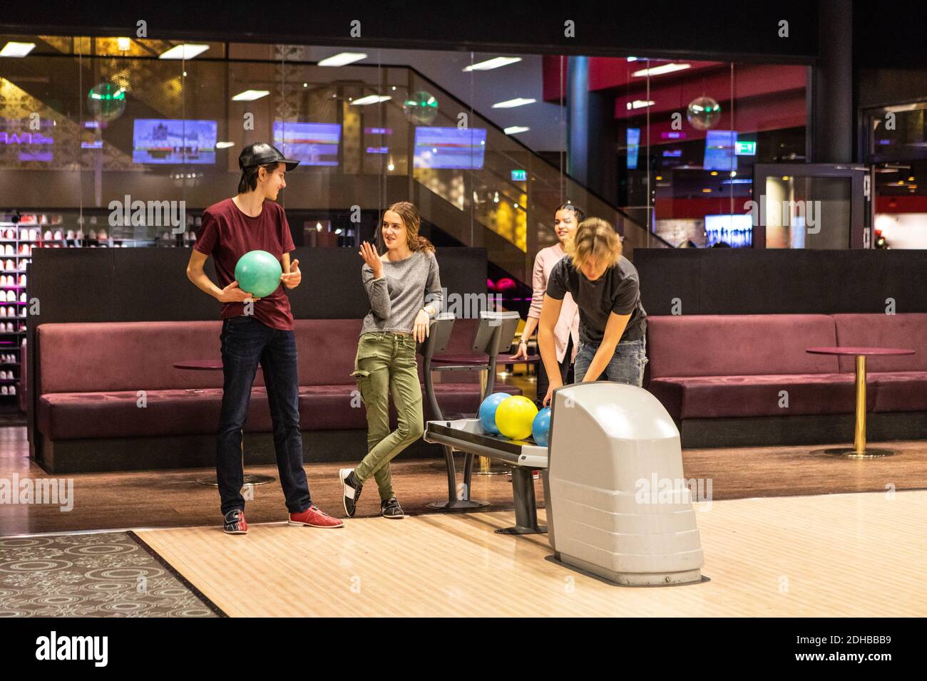 Smiling teenage friends playing on illuminated parquet floor at bowling ...