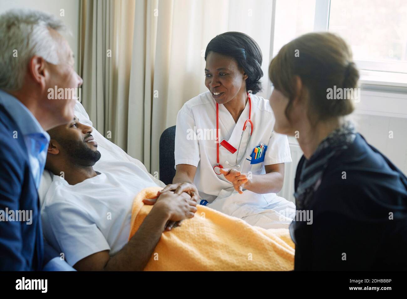 Healthcare worker encouraging patient and his family at hospital ward ...
