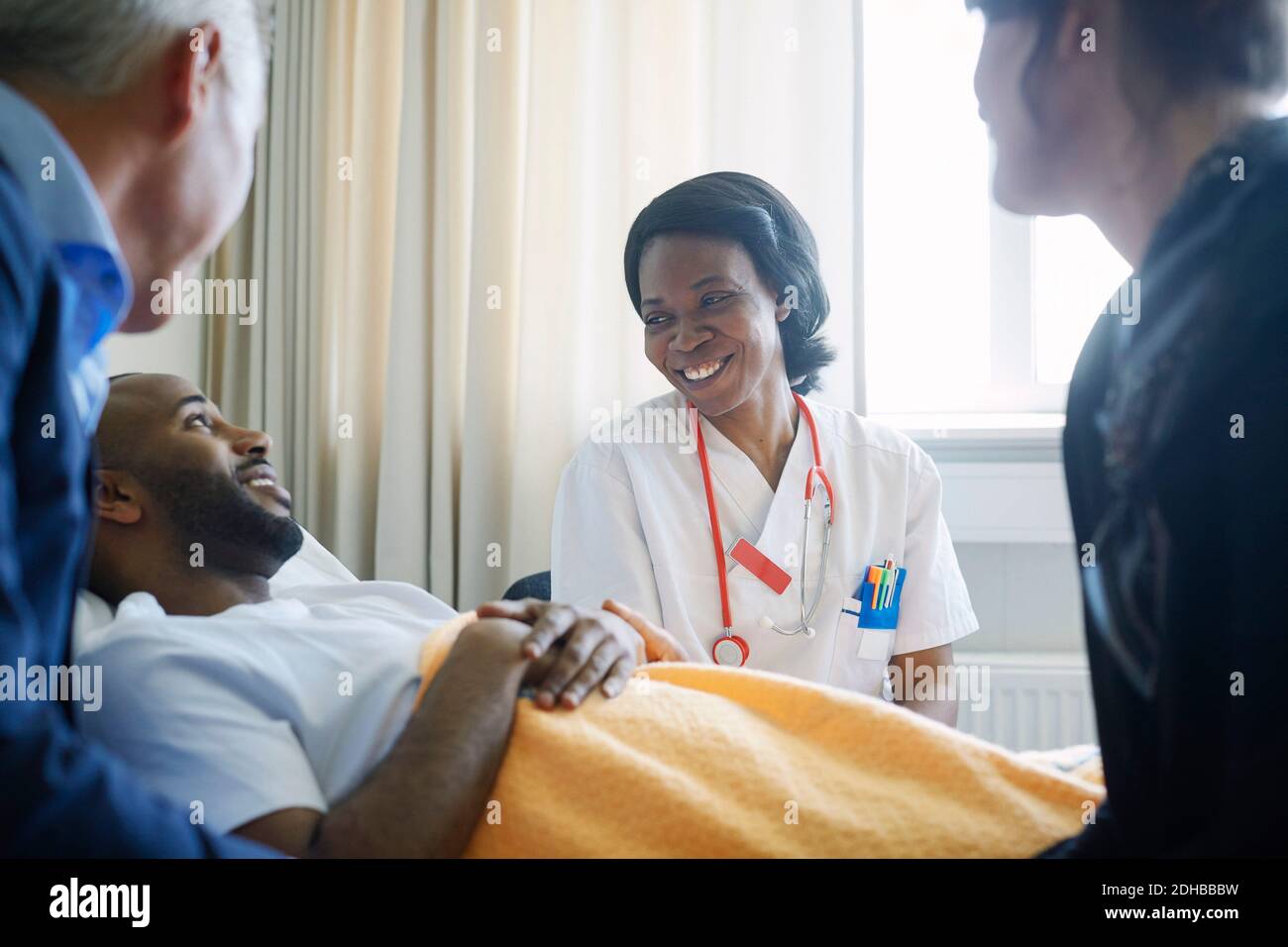 Smiling female doctor talking to patient and family in hospital ward ...