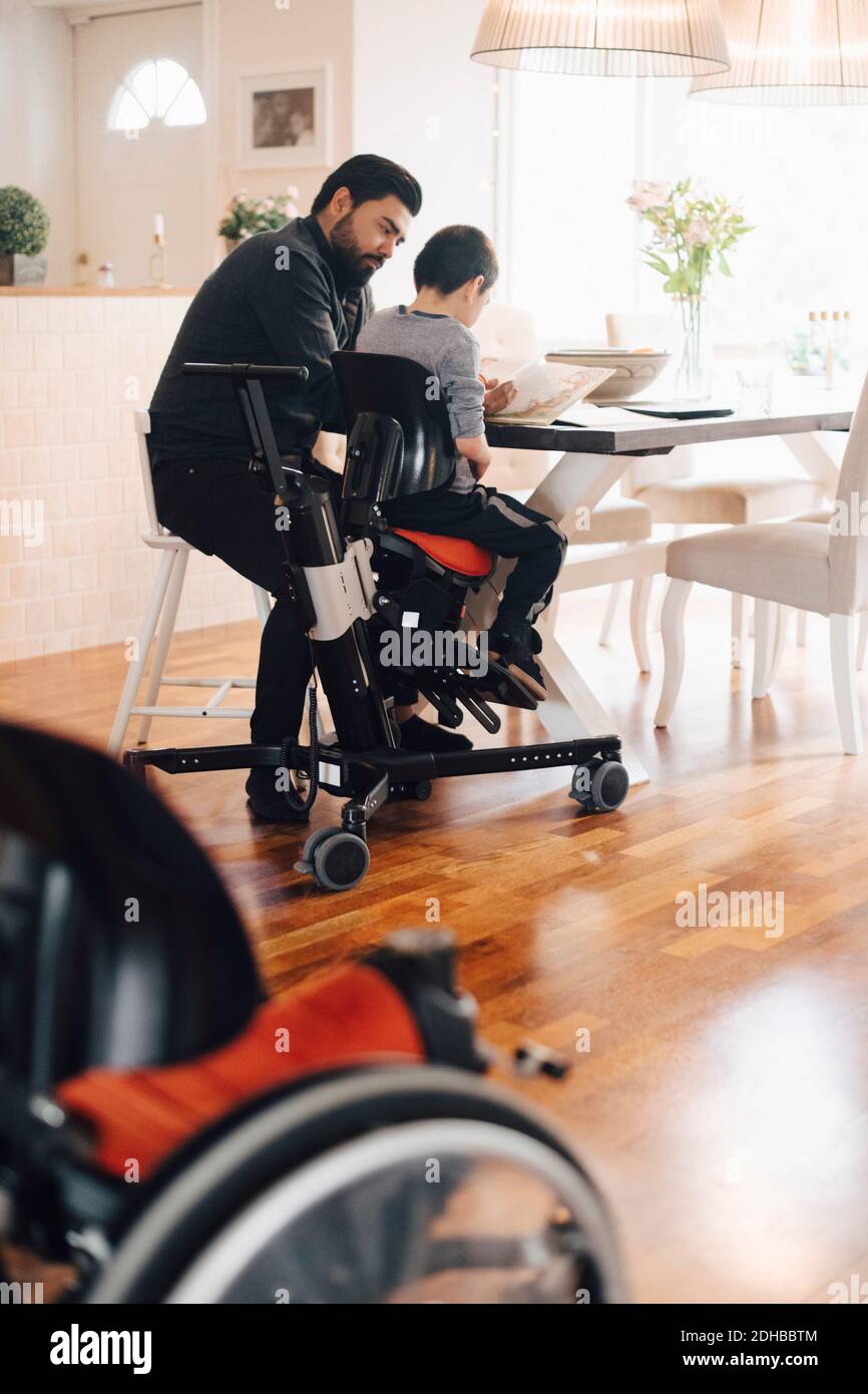 Side view of father teaching autistic son while sitting at table in ...