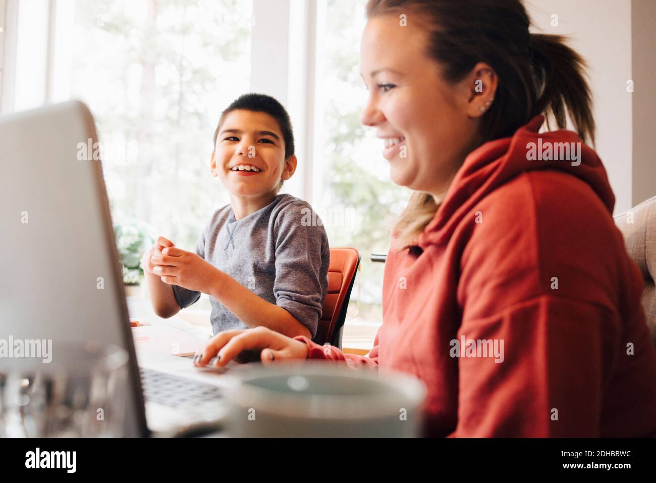 Mother using laptop while sitting with happy autistic son in living ...