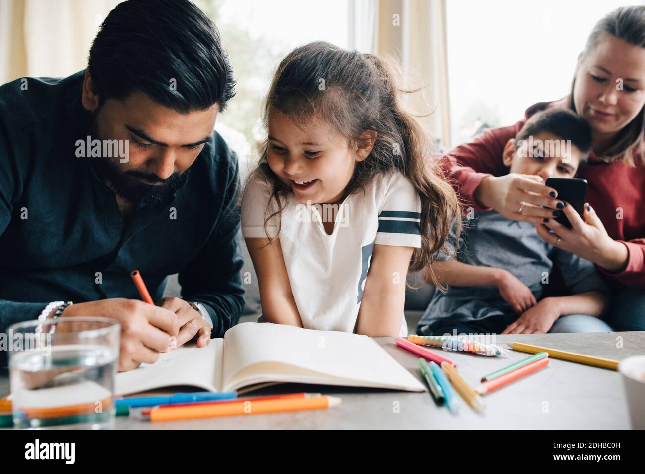 Father teaching drawing to daughter while woman using smart phone with ...