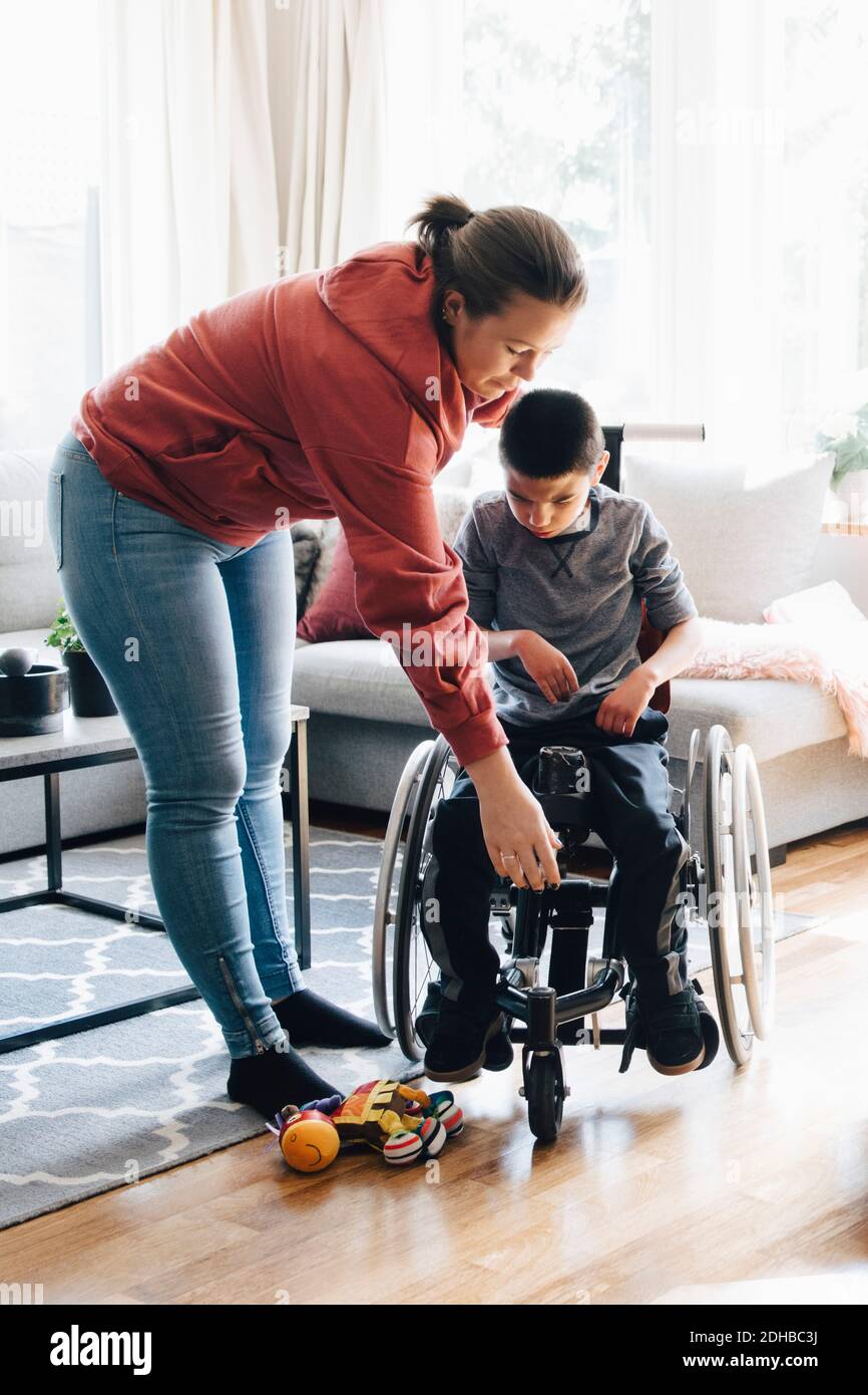 Mother assisting autistic son in sitting on motorized wheelchair at ...