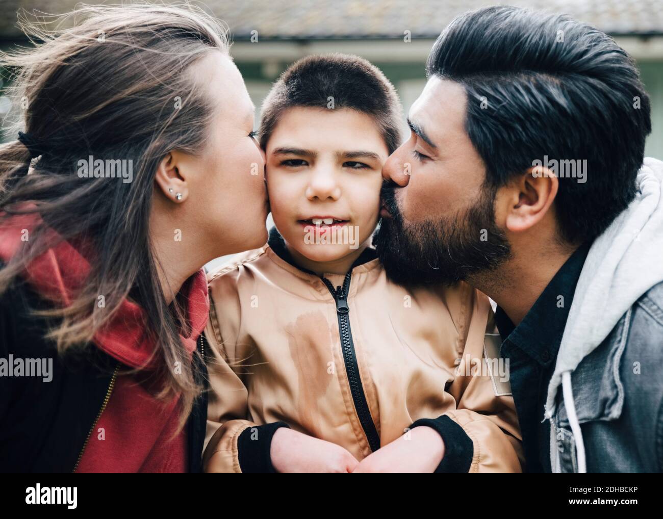Side view of parents kissing autistic son in yard Stock Photo - Alamy