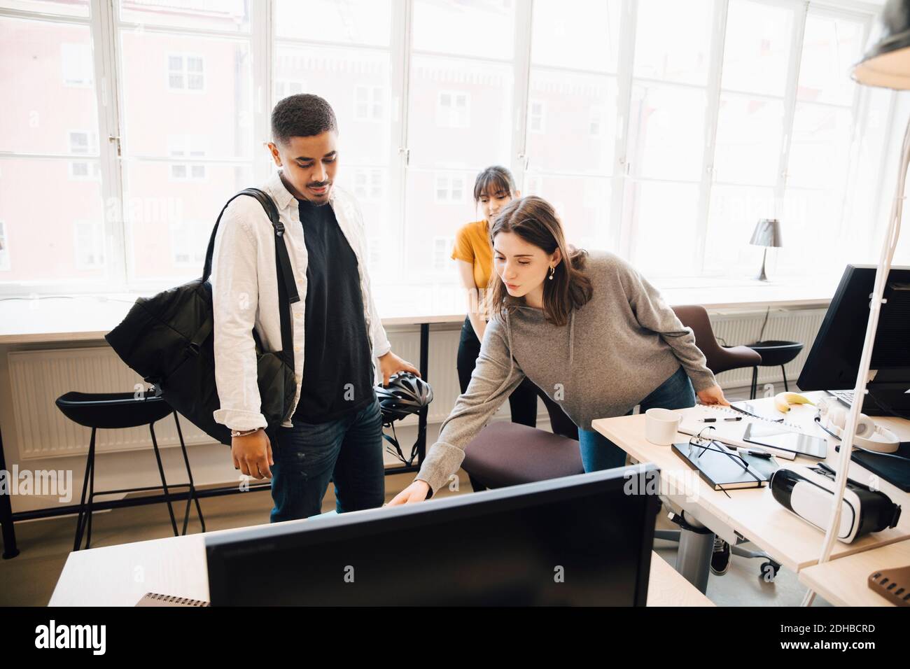 Female programmer showing computer to coworkers against window in ...