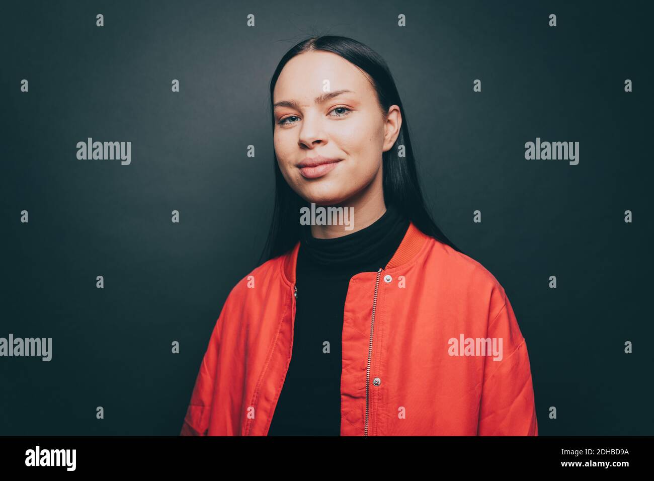 Portrait of woman smiling while wearing orange jacket over gray ...