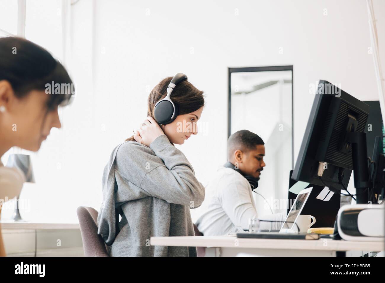 Focused female programmer with headphones using laptop on desk while ...