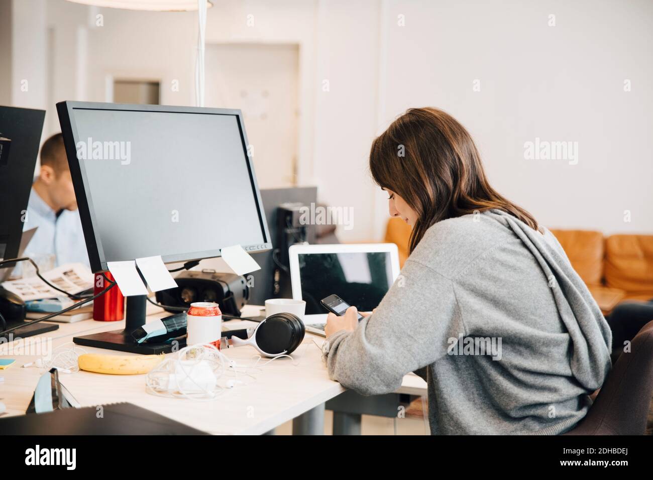 Side view of female programmer using mobile phone on desk while sitting ...