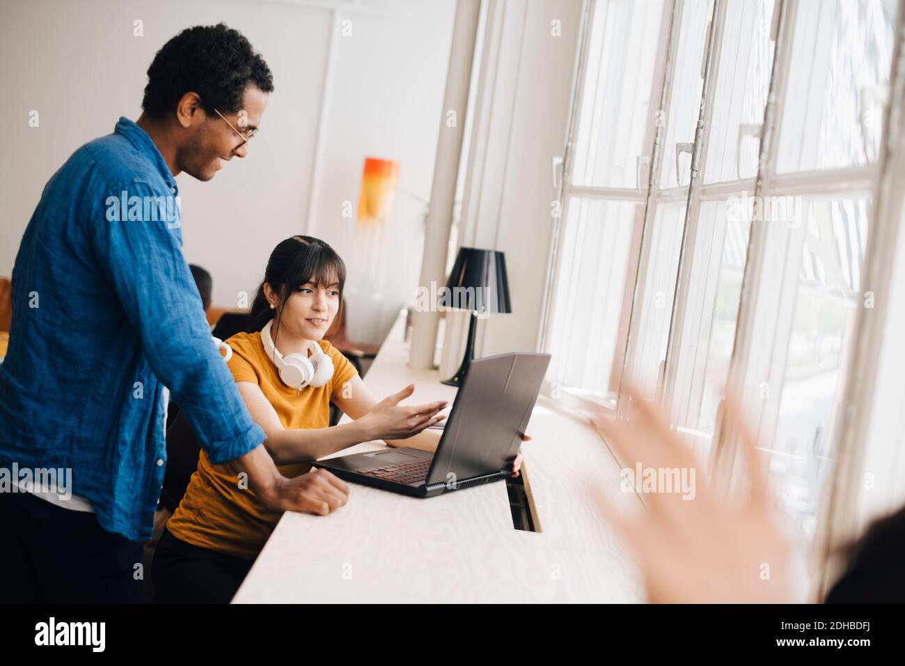 Female programmer explaining to male coworker over laptop on desk in ...