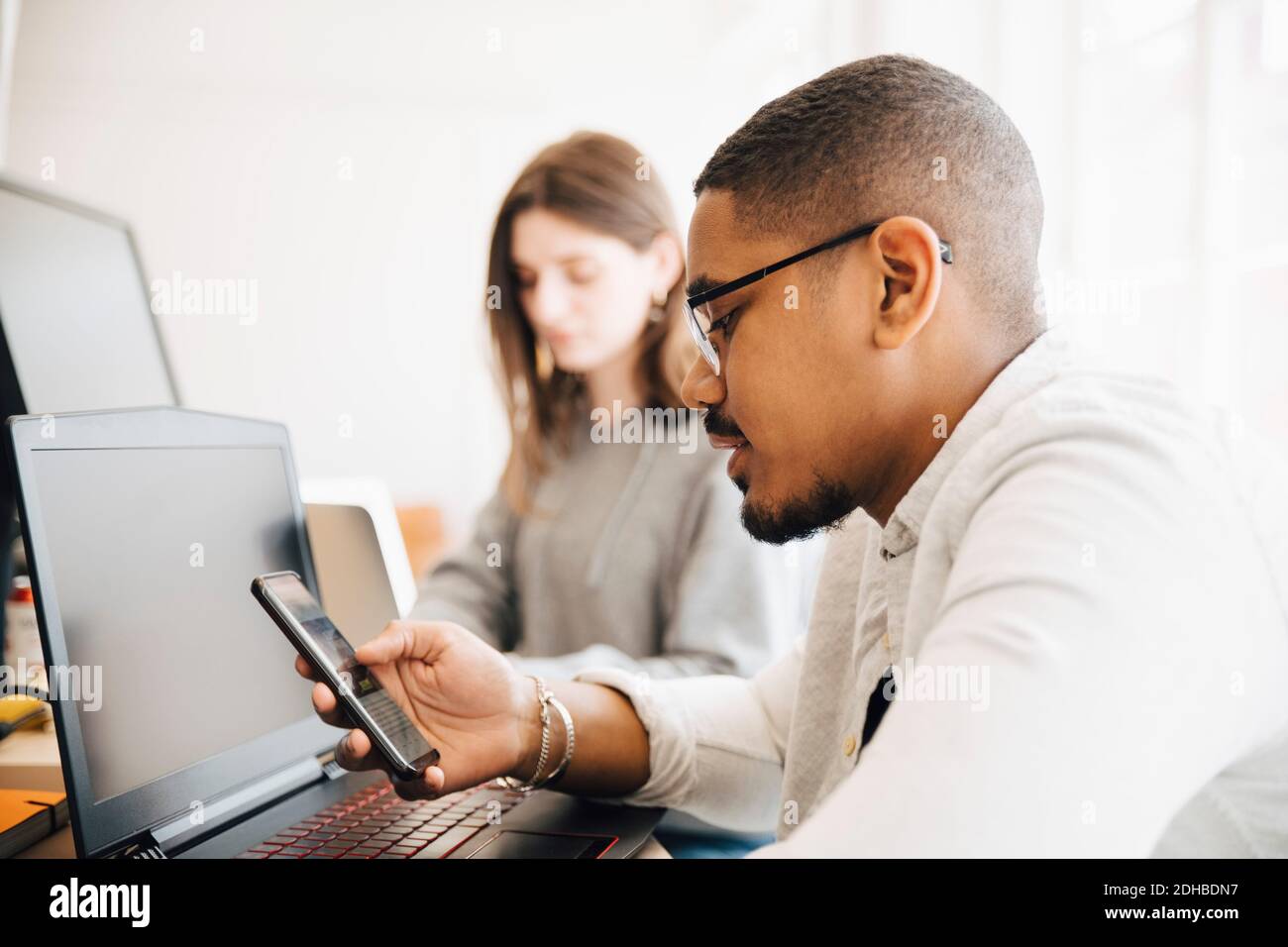 Male computer programmer using smart phone while sitting by female ...