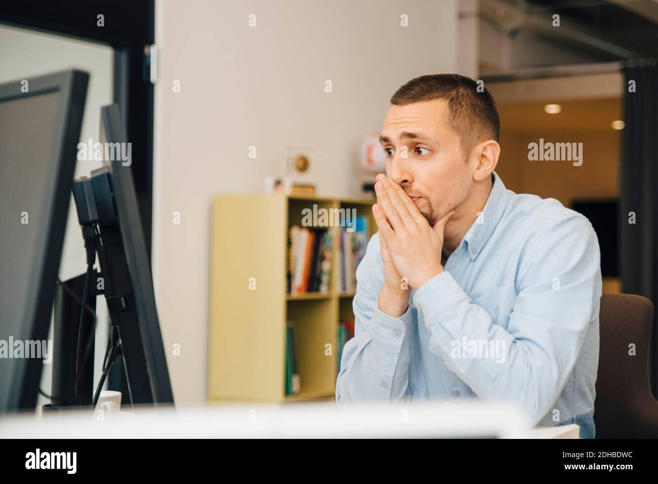 Thoughtful programmer with hands clasped looking at computer monitor ... Thoughtful programmer with hands clasped looking at computer monitor ...