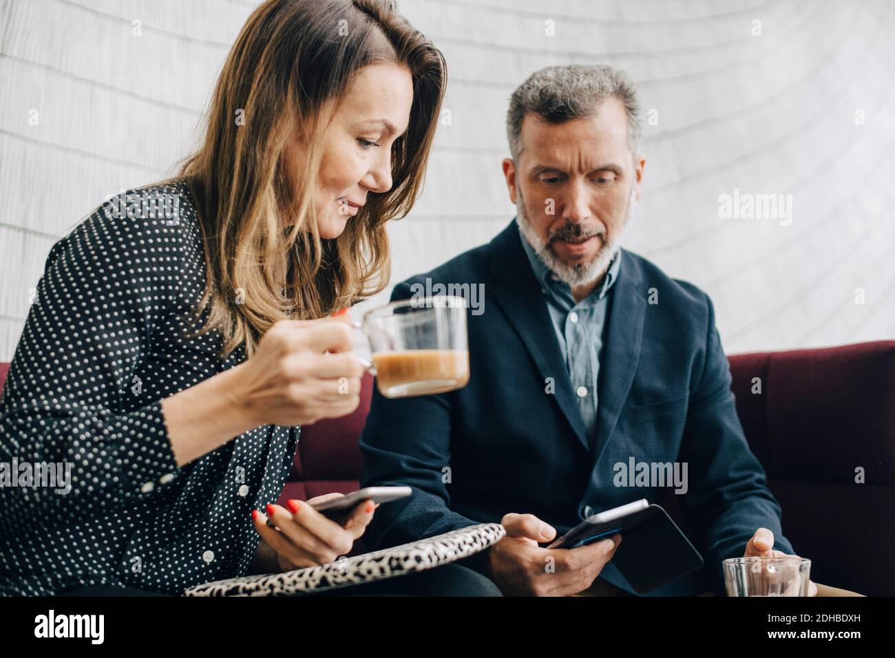 Business colleagues using phones and having tea while sitting on couch ...