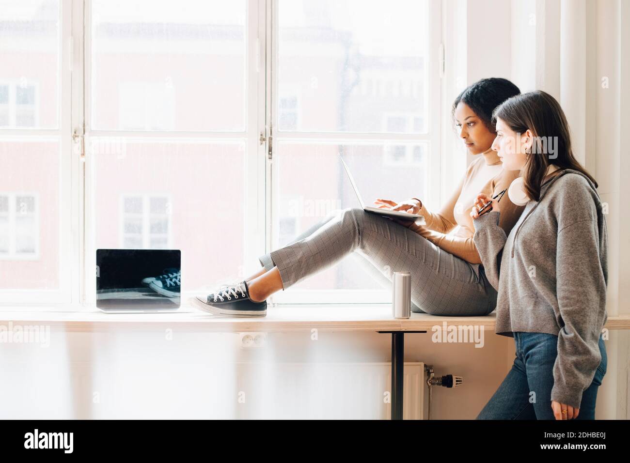 Computer programmers discussing over laptop while working by window in ...