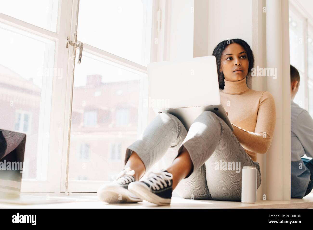 Full length of female computer programmer looking away while sitting by ...