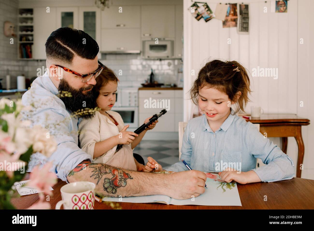 Father assisting girl in homework while sitting with daughter at dining table Stock Photo - Alamy