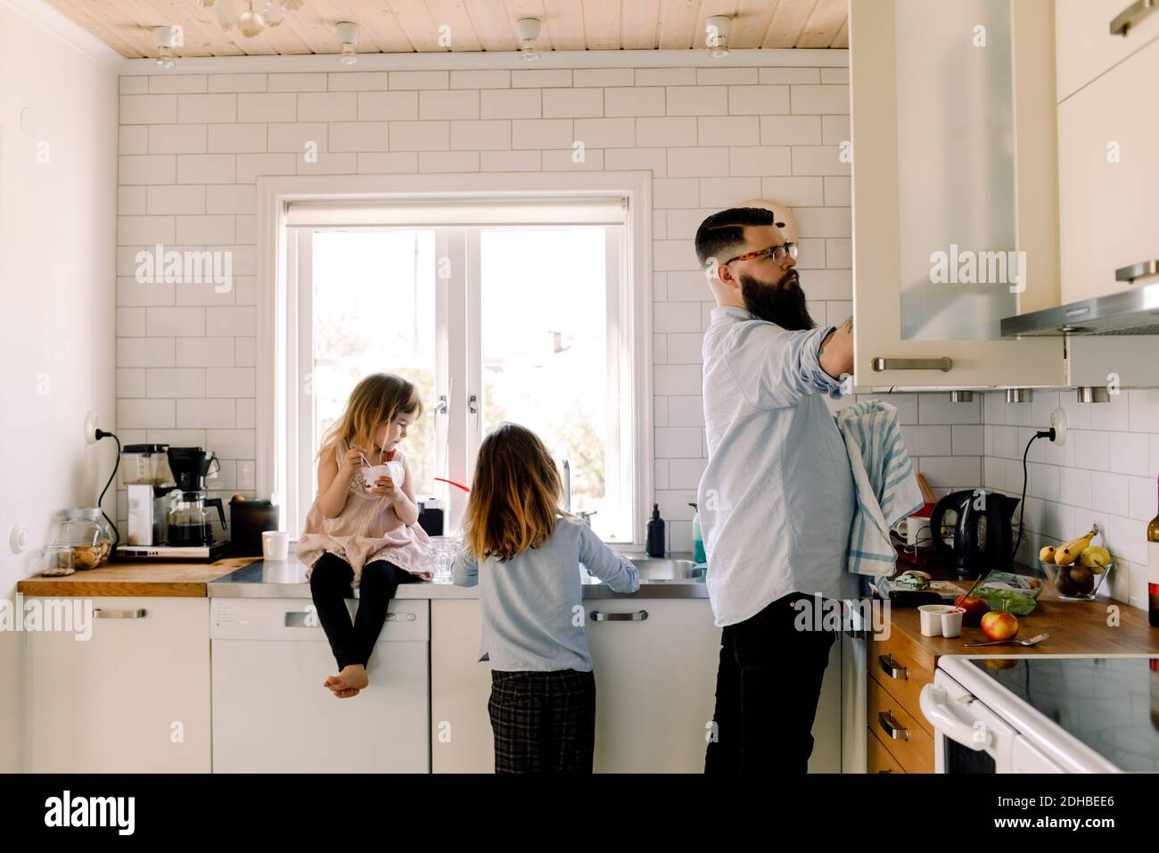 Girl looking at working sister while father doing chores in kitchen ...