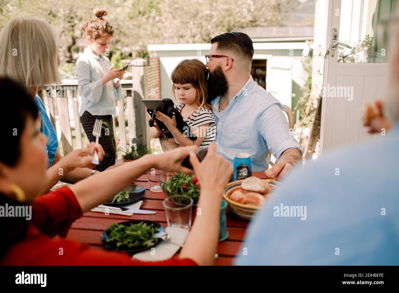 Multi-generational family having food while daughters using technology ...