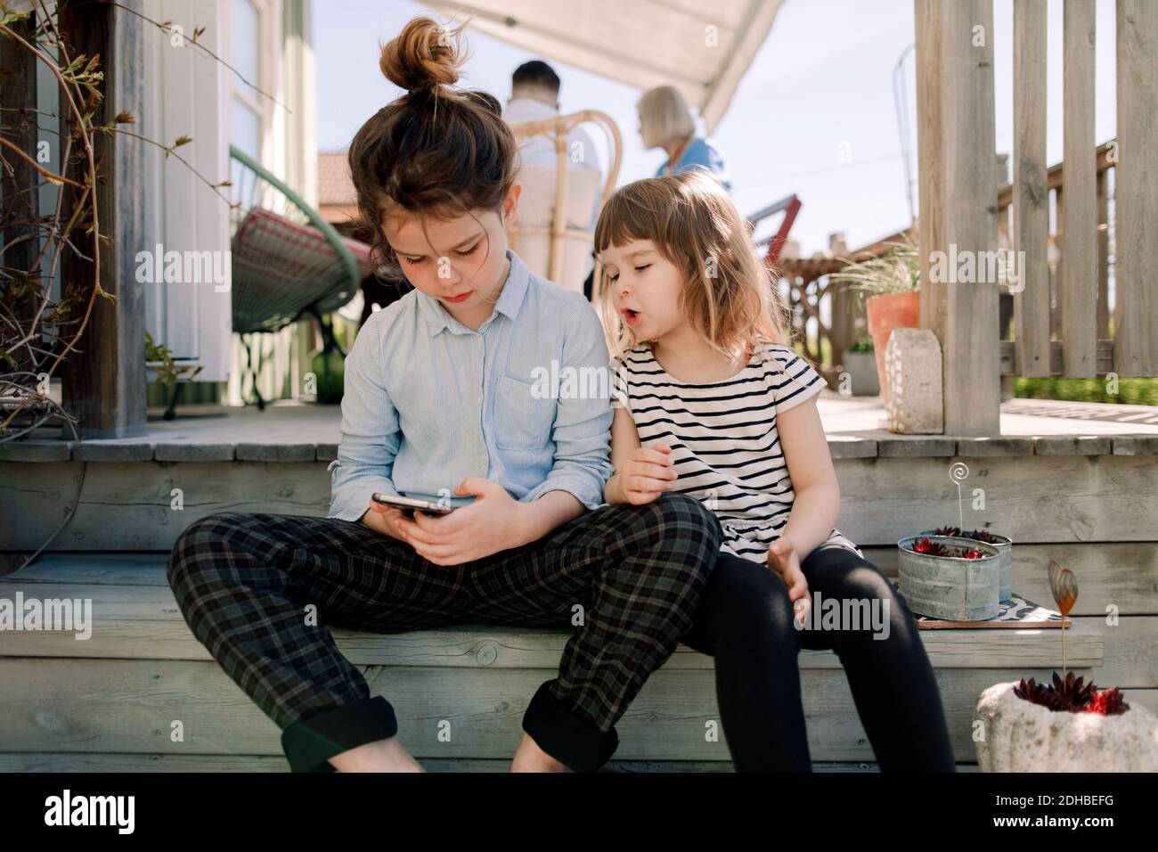 Girl talking to sister using smart phone while sitting on steps in ...