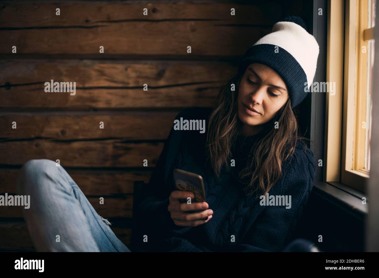 Woman using mobile phone while sitting in log cabin Stock Photo - Alamy